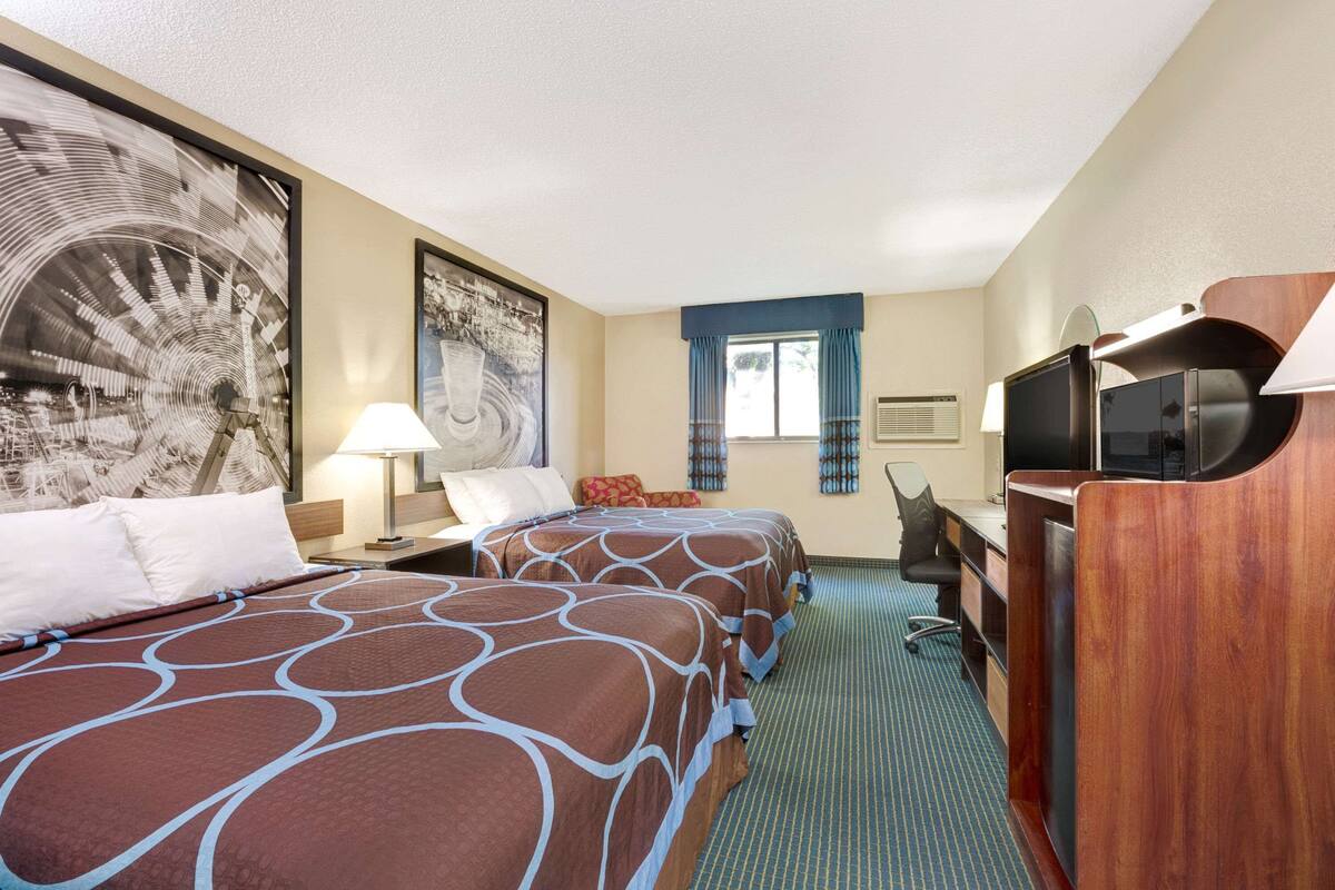 Quarto de hotel com duas camas, uma mesa de trabalho com televisão e um quadro grande na parede.
