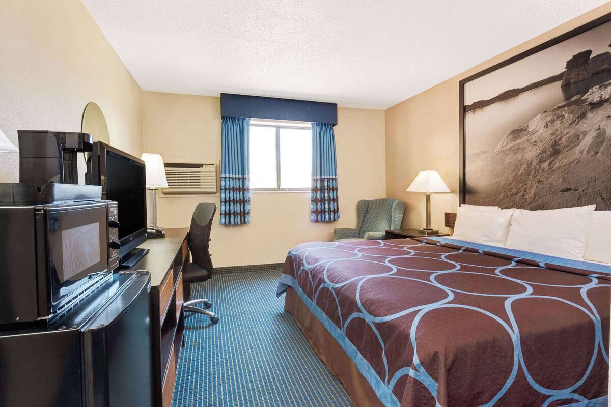 Quarto de hotel com cama, escrivaninha com computador, televisão e micro-ondas.