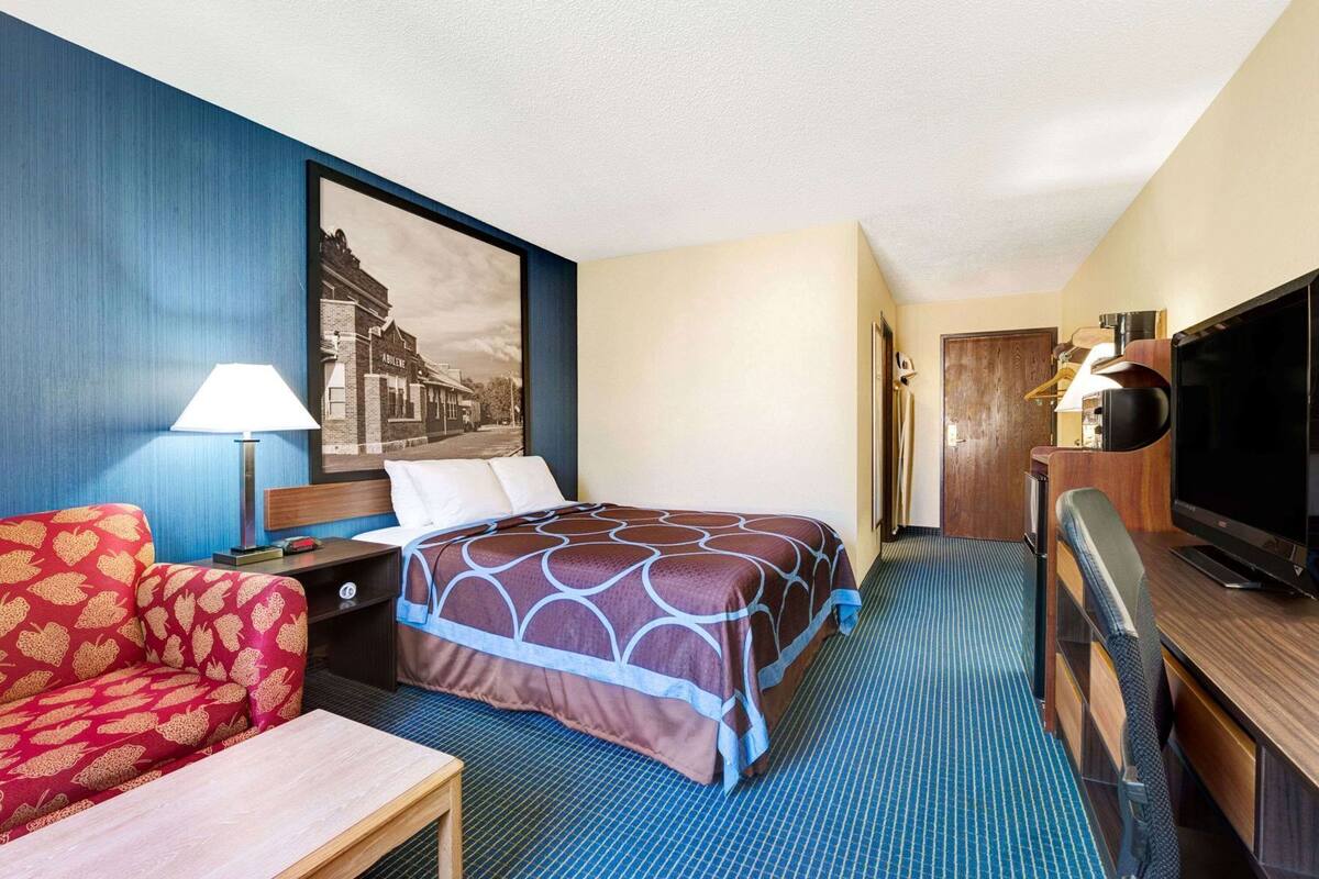 Quarto de hotel com uma cama, escrivaninha, televisão, poltrona e sofá.