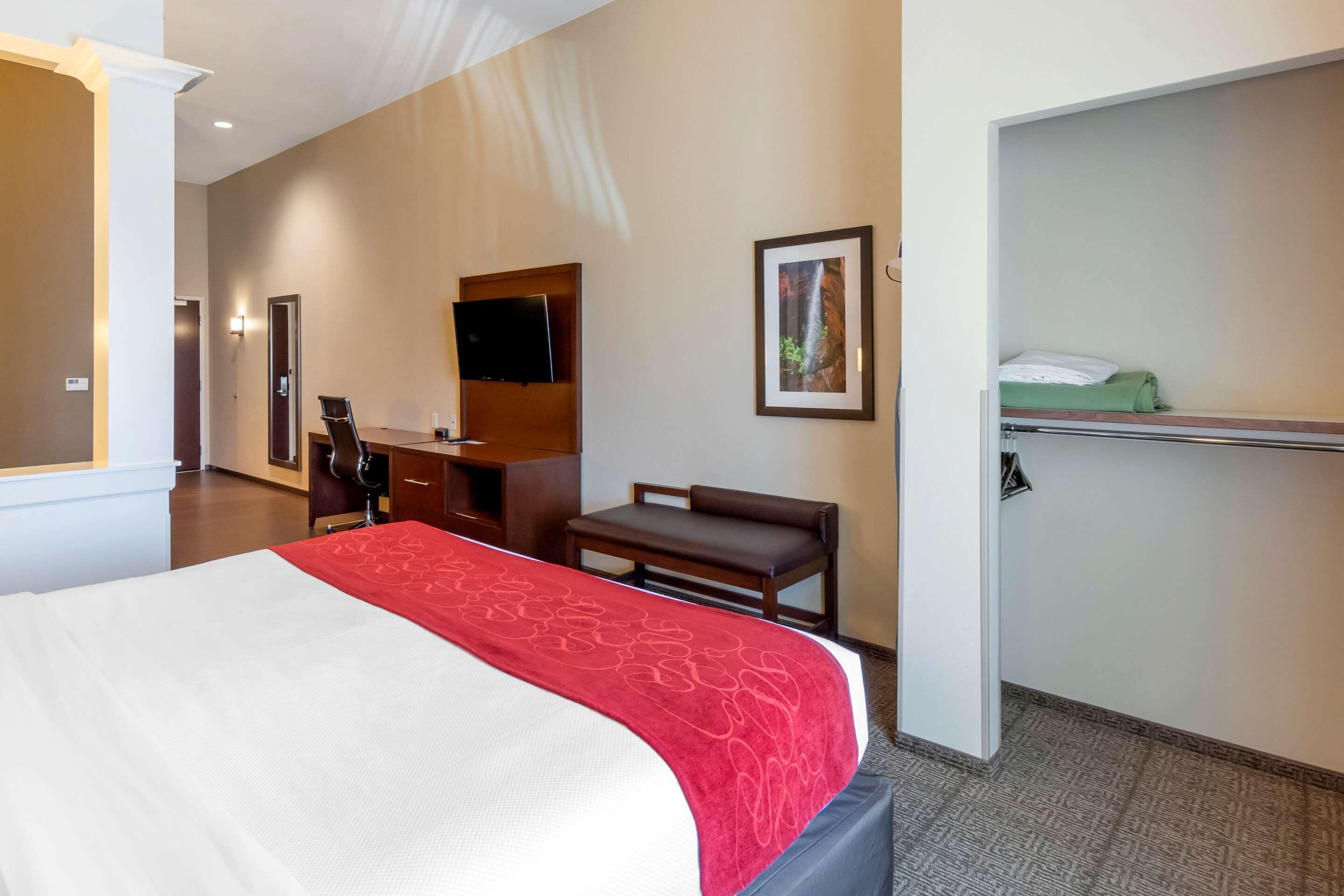 Quarto de hotel com cama, escrivaninha, cadeira, televisão e um quadro na parede.