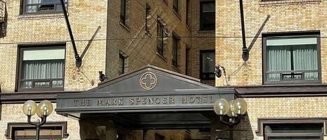 Um edifício de tijolos com uma placa indicando "The Mark Spencer Hotel". Há cestos de flores no chão e uma placa que indica uma zona hoteleira.