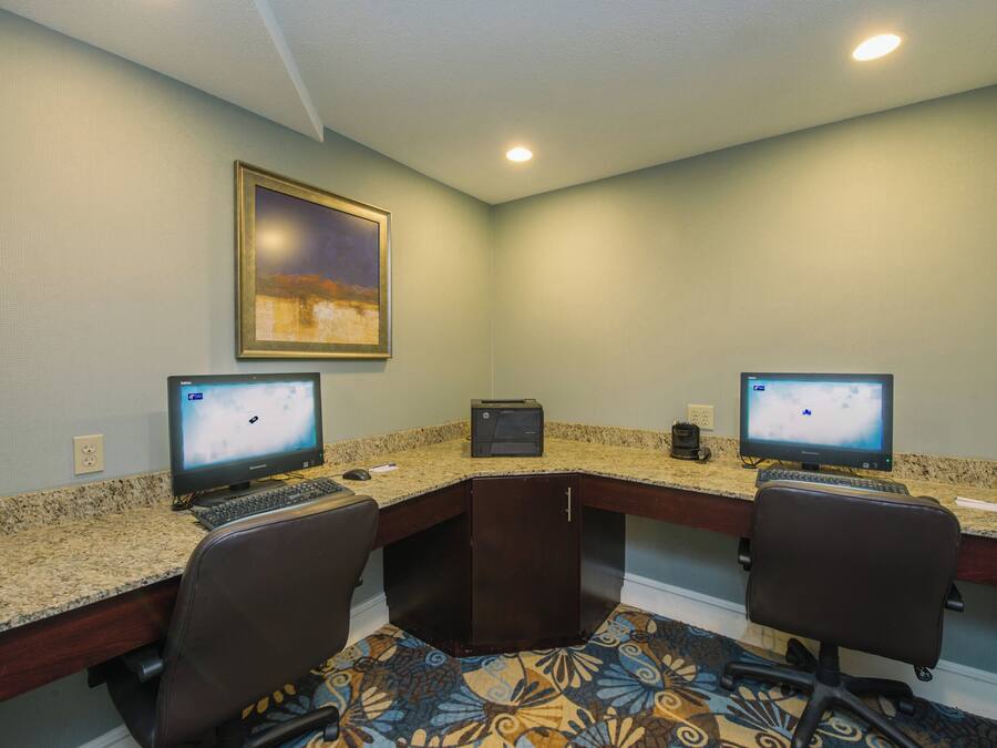 Sala de conferências com duas mesas, cada uma equipada com um computador, uma impressora e uma cadeira.