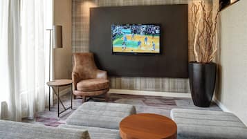 Uma sala de estar moderna com televisão de tela plana, uma poltrona de couro, uma mesa de centro redonda de madeira e um vaso grande com galhos.