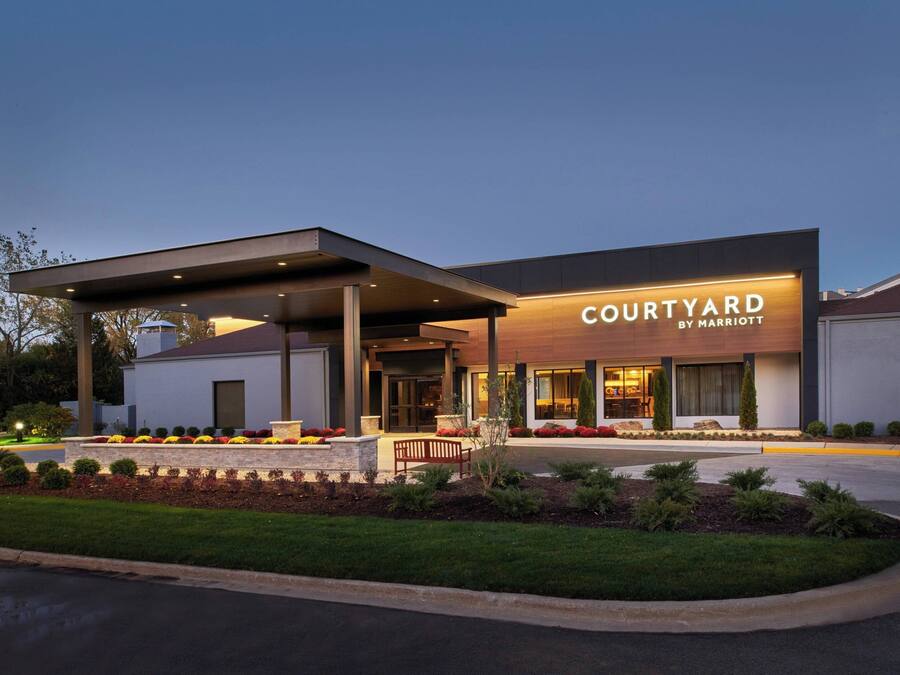 Um hotel Courtyard by Marriott com entrada coberta, jardim ajardinado e fachada bem iluminada.