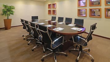 Sala de conferência com mesa redonda, seis cadeiras e um vaso de plantas.