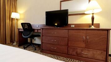 Quarto de hotel com cama, escrivaninha com computador, televisão, poltrona, armário e duas luminárias.