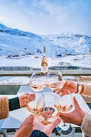 Paisagem montanhosa nevada com um teleférico, uma mesa com uma garrafa de vinho e vários copos.
