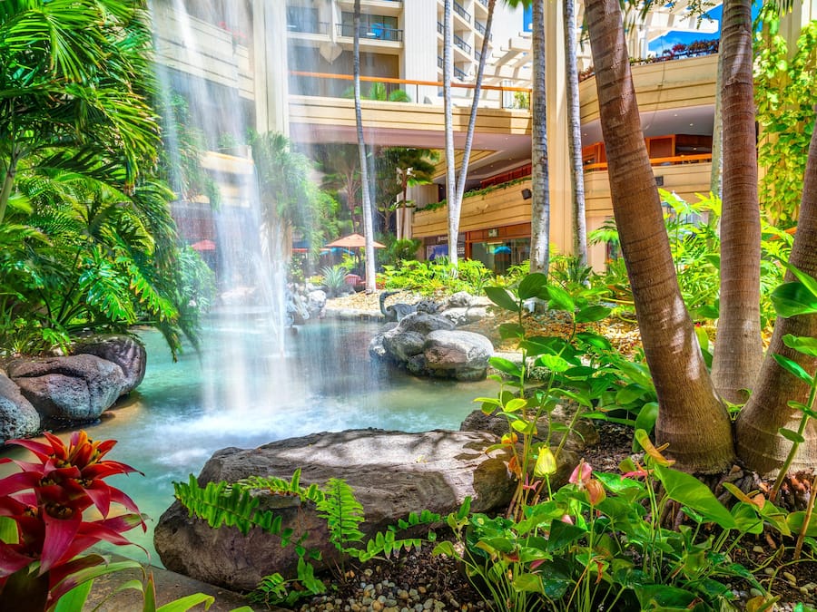 Um átrio de hotel com cascata, plantas internas e vista do interior do edifício.