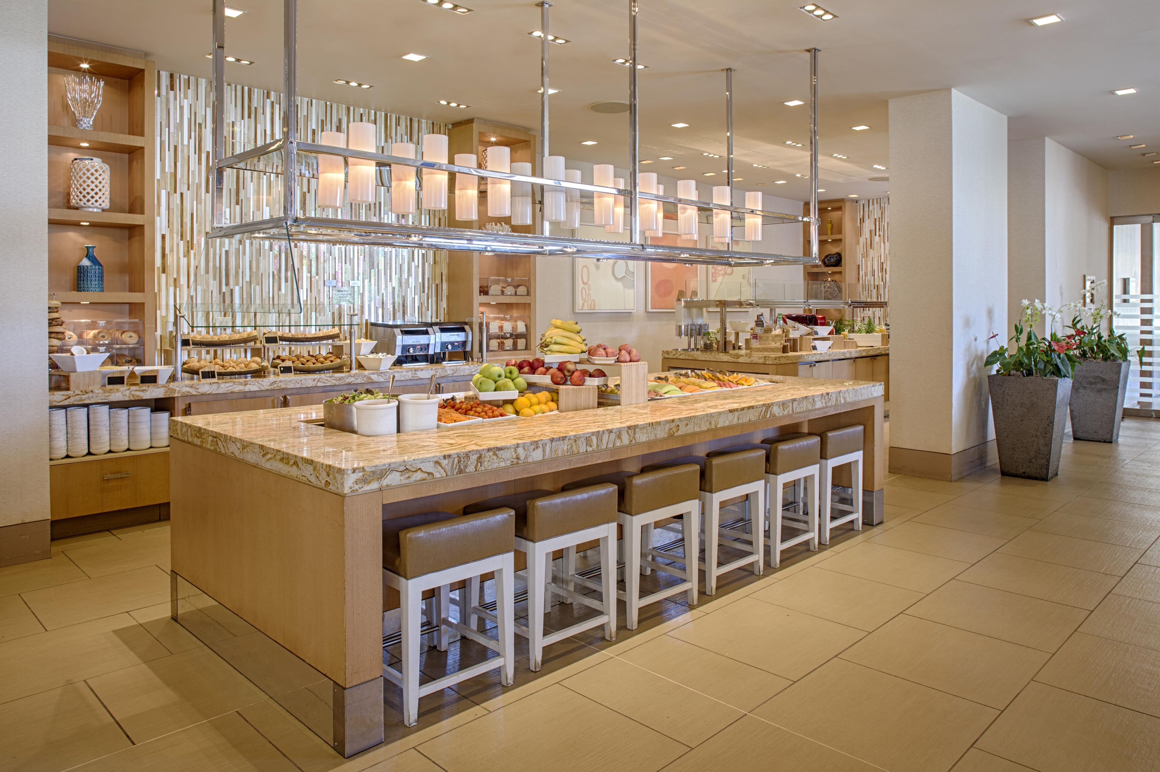 Cozinha moderna com bancada de mármore, banquetas e diversos alimentos.