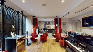 Uma sala de estar moderna com um piano, cadeiras vermelhas e uma área de cozinha ao fundo.