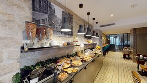 Uma área de buffet com diversos alimentos e acompanhamentos, um espaço de refeições com mesas e cadeiras, e um mural com vista para a cidade na parede.
