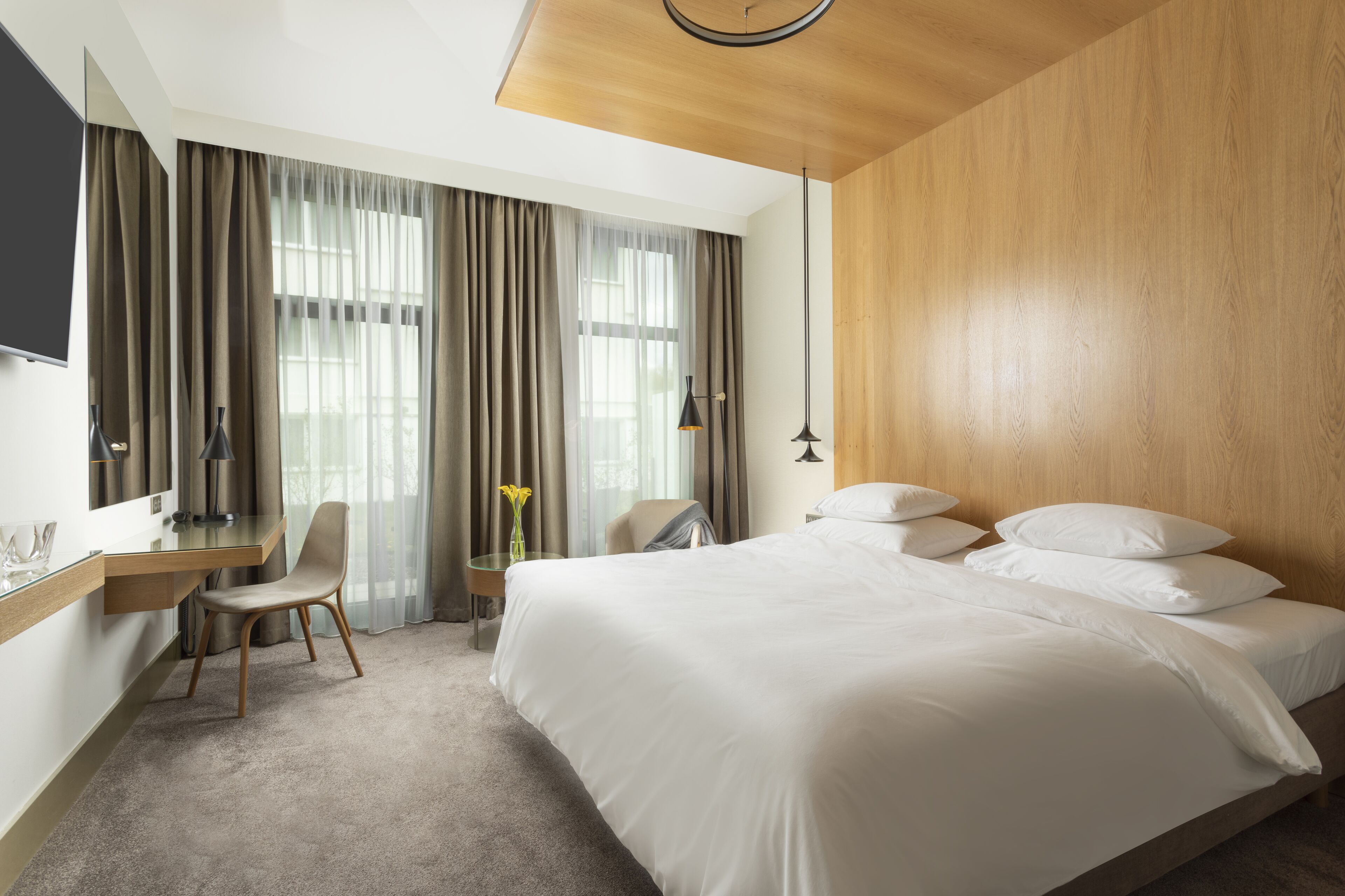 Quarto de hotel com cama, escrivaninha, cadeira, televisão e janela com cortinas.
