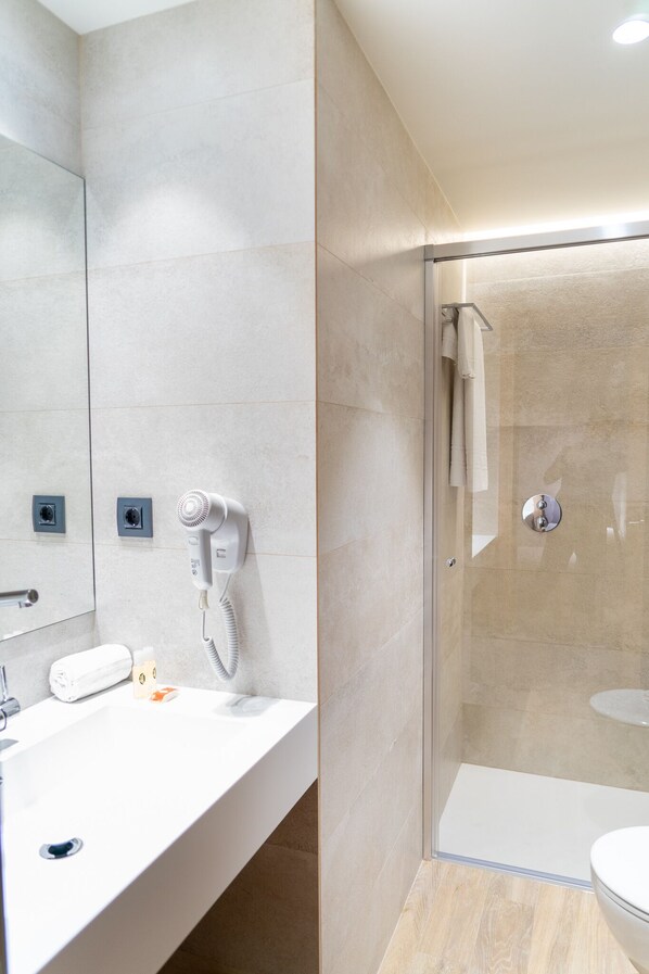 Uma casa de banho moderna com uma sanita branca, secador de cabelo e cabine de duche em vidro.