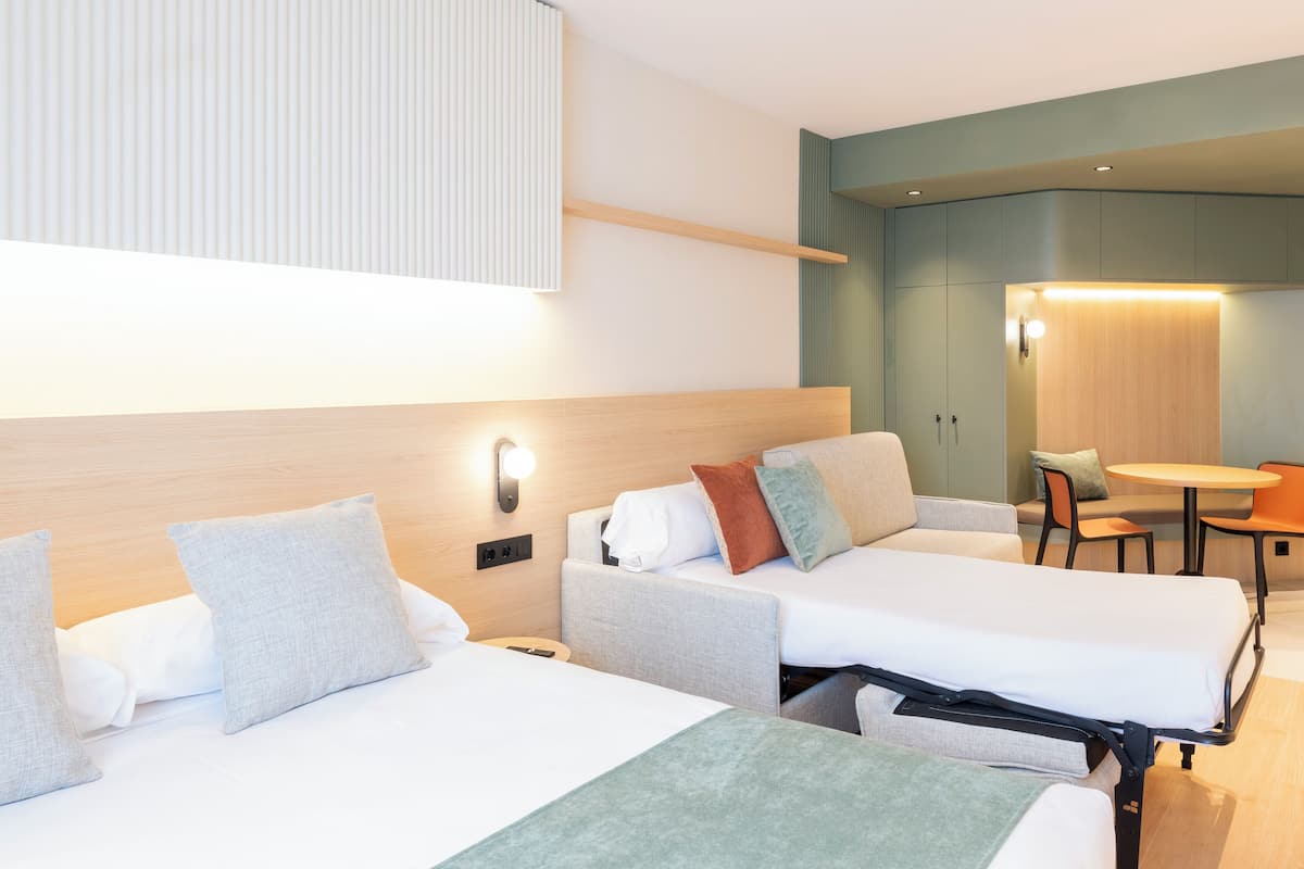 Quarto de hotel com duas camas, uma mesinha e um espaço de estar.