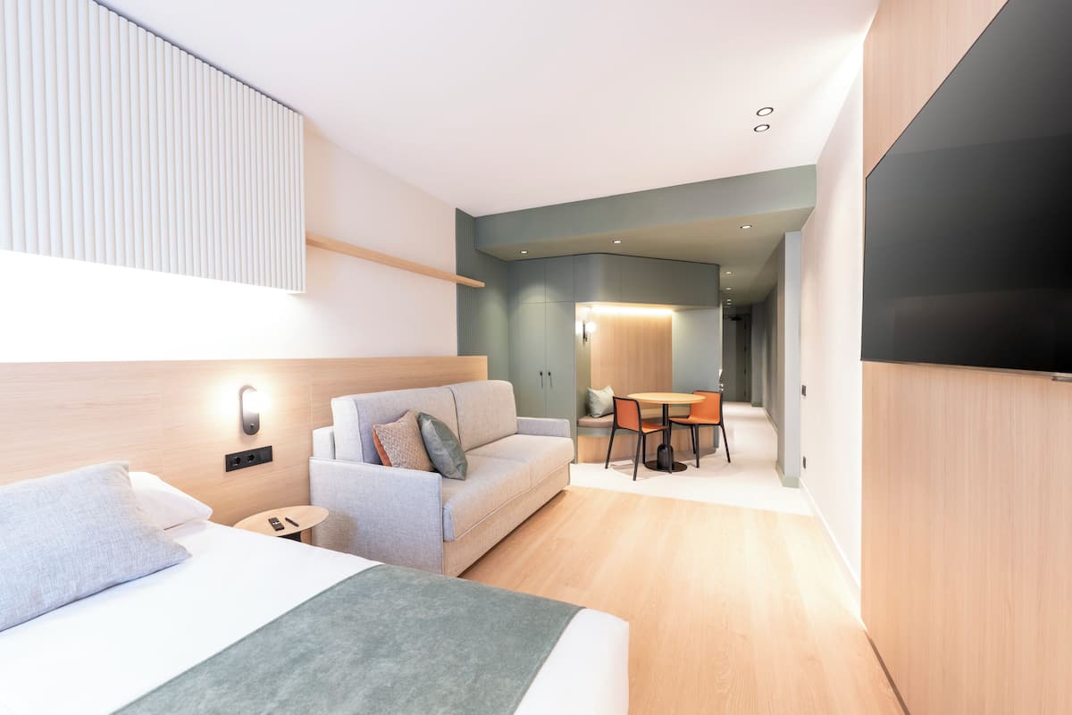 Quarto de hotel moderno com uma cama, um sofá, uma mesinha e uma televisão.