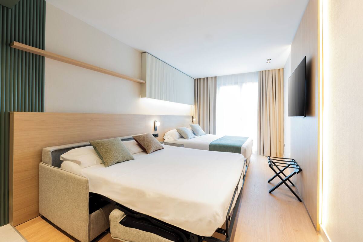 Quarto de hotel moderno com duas camas, uma televisão de tela plana e uma estante embutida.