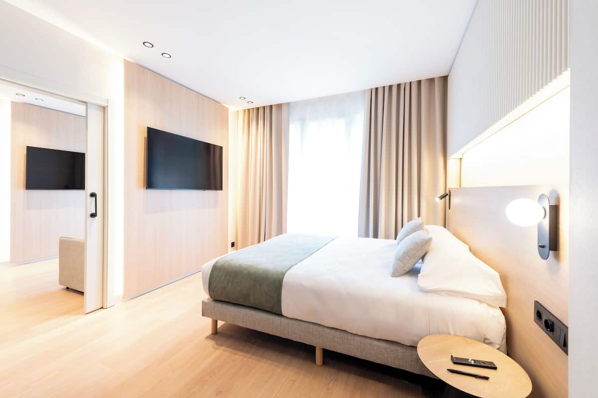 Quarto de hotel moderno com uma cama grande, uma televisão de tela plana na parede, uma mesa de cabeceira e um closet espaçoso.