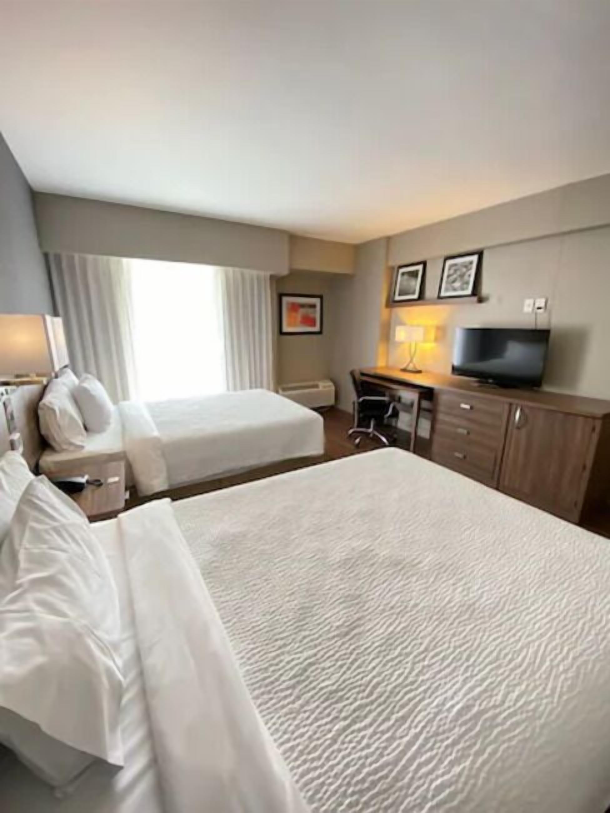 Quarto de hotel com uma cama grande, uma escrivaninha com cadeira, televisão e janela com cortinas.