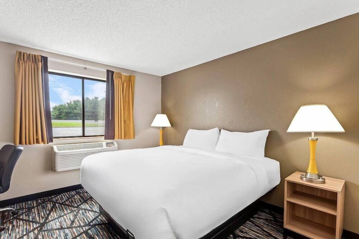 Quarto de hotel com cama, duas luminárias de cabeceira, uma cadeira, escrivaninha e vista para o exterior.