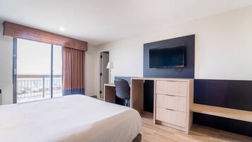 Quarto de hotel com cama, escrivaninha, cadeira, televisão e varanda com cortinas.