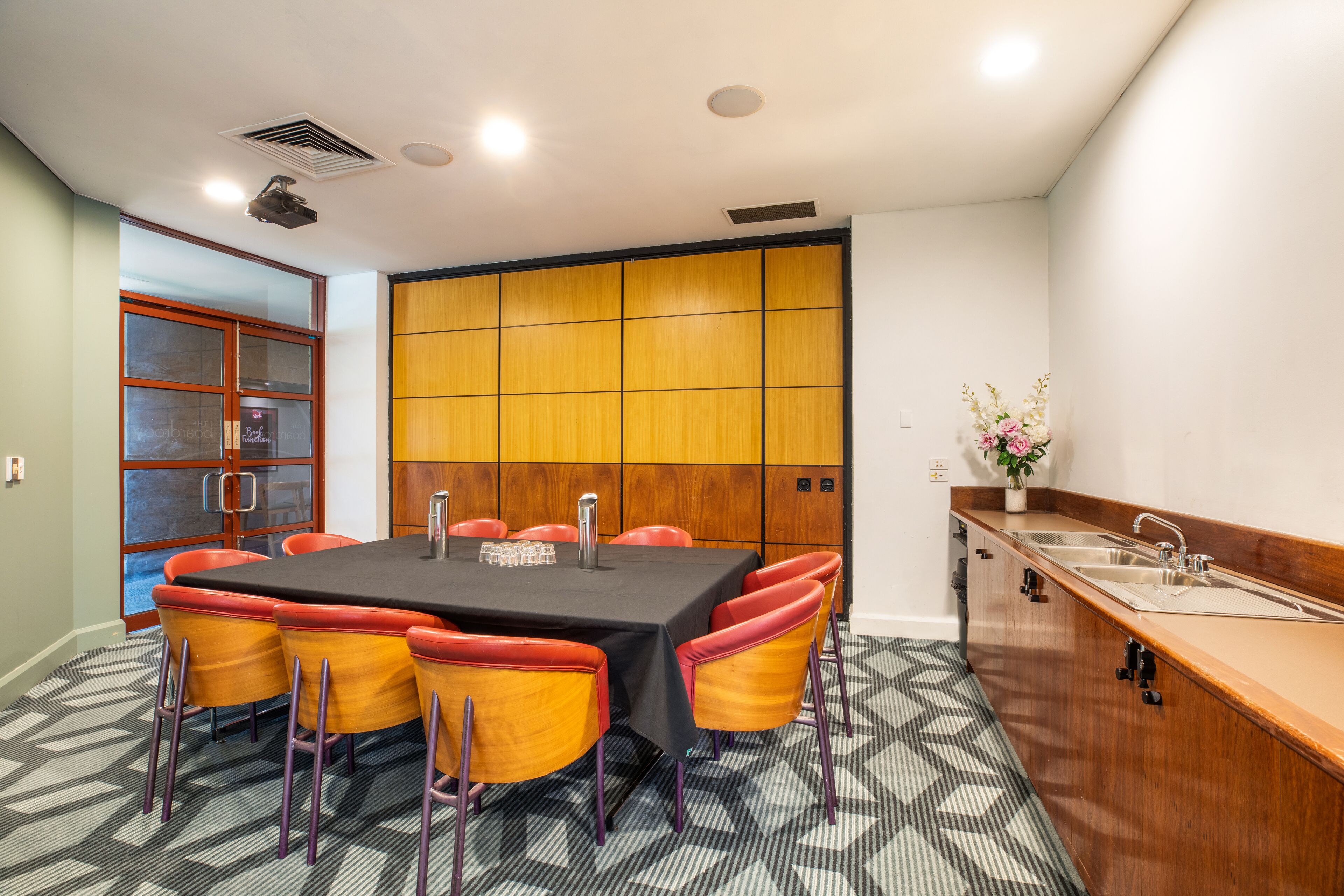 Uma sala de conferências com mesa, cadeiras e uma área de cozinha com pia e armários.