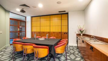 Uma sala de conferências com mesa, cadeiras e uma área de cozinha com pia e armários.