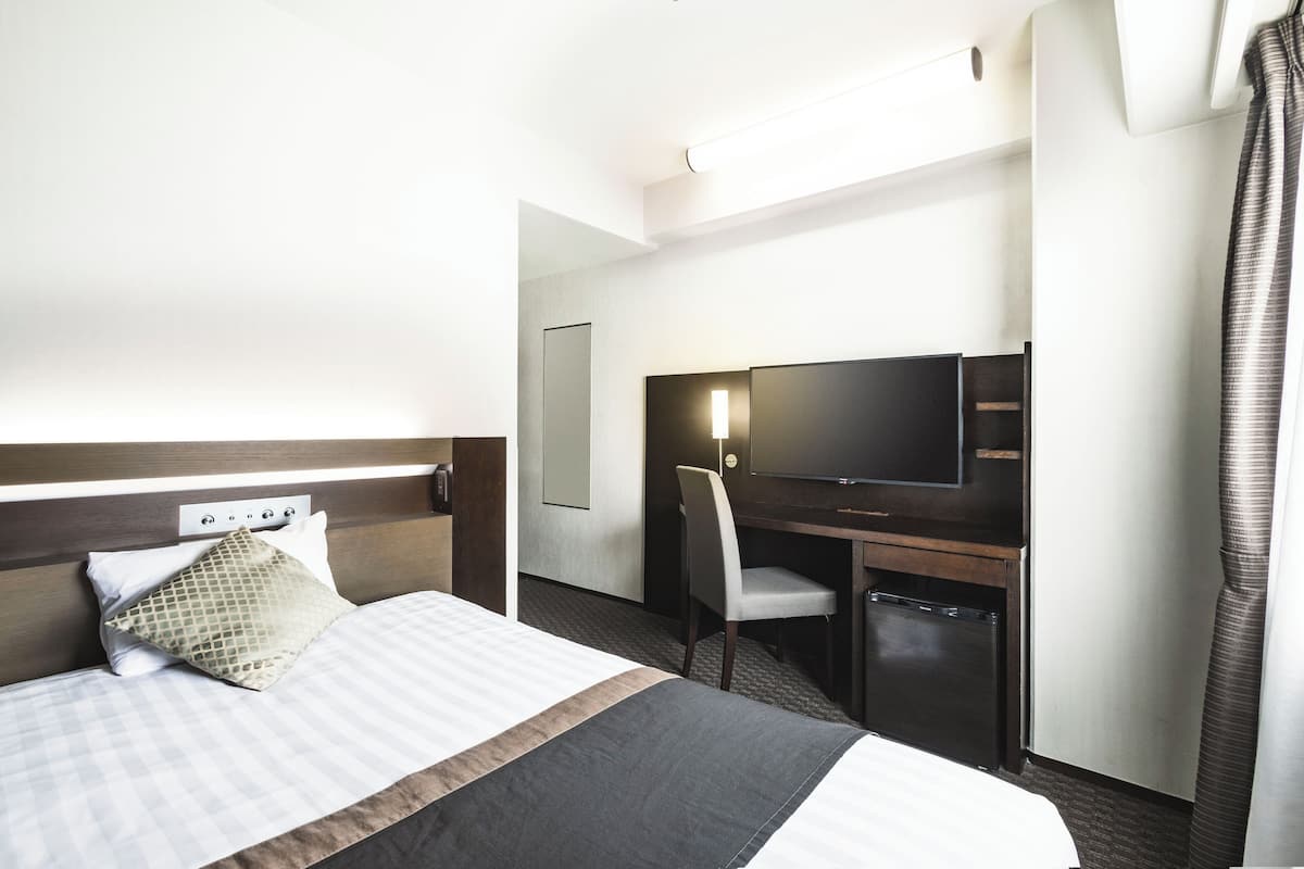 Quarto de hotel com cama, secretária com televisão, cadeira e armário.