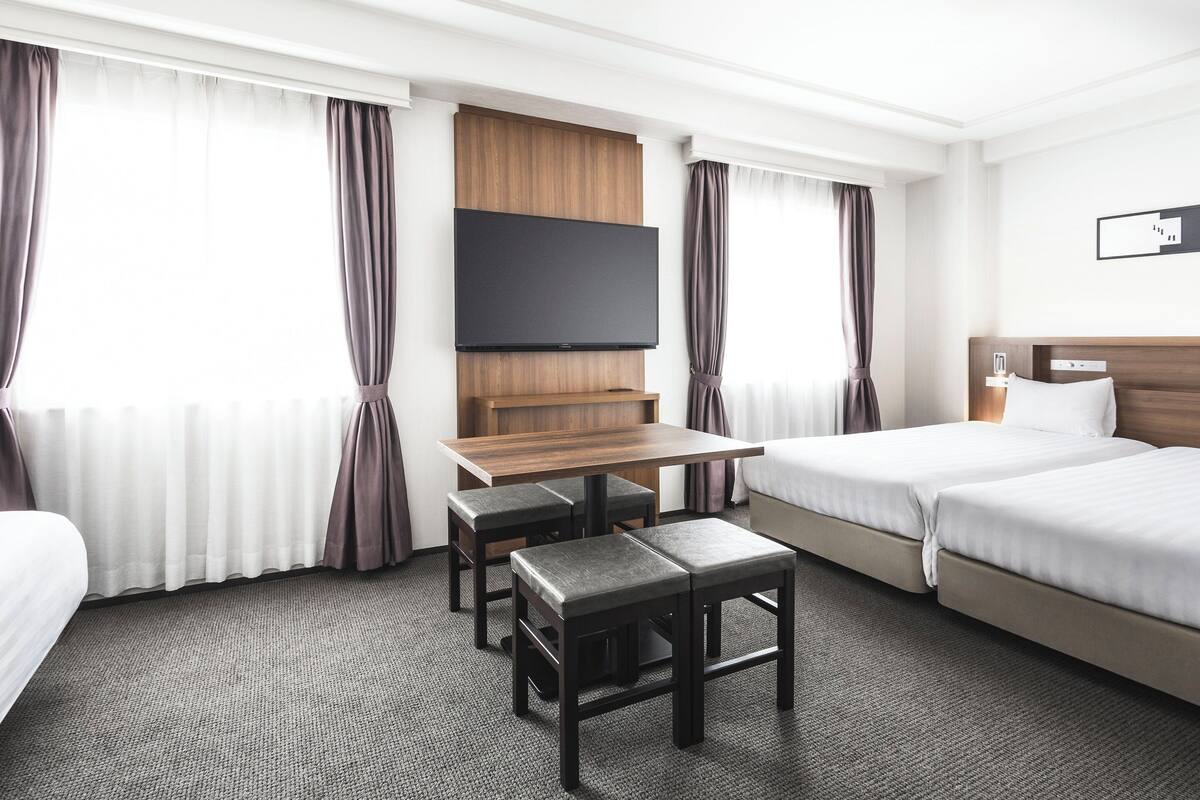 Quarto de hotel com duas camas, televisão, escrivaninha e uma cadeira.