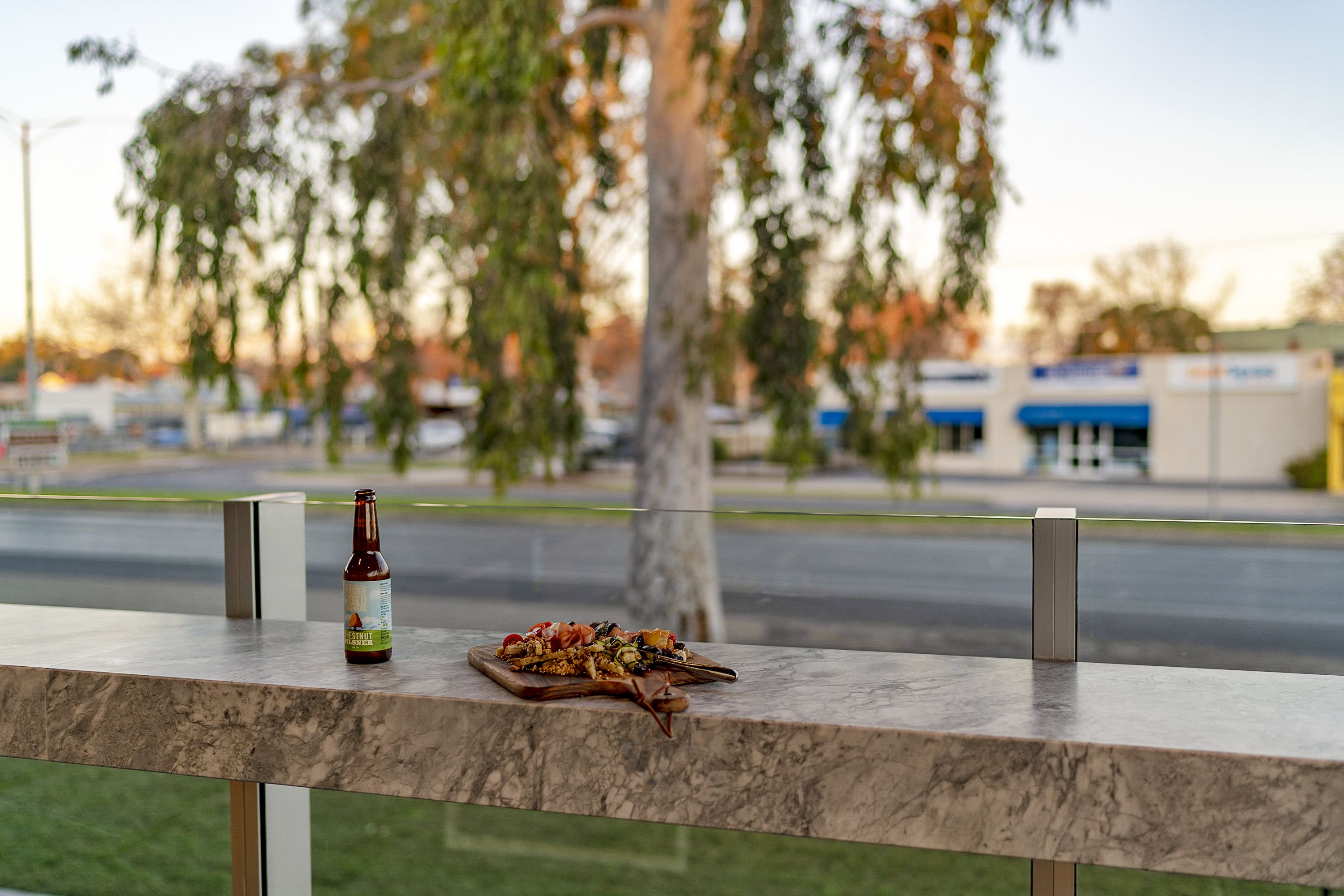 Uma mesa com garrafa e comida, com vista para uma rua com árvores e edifícios.