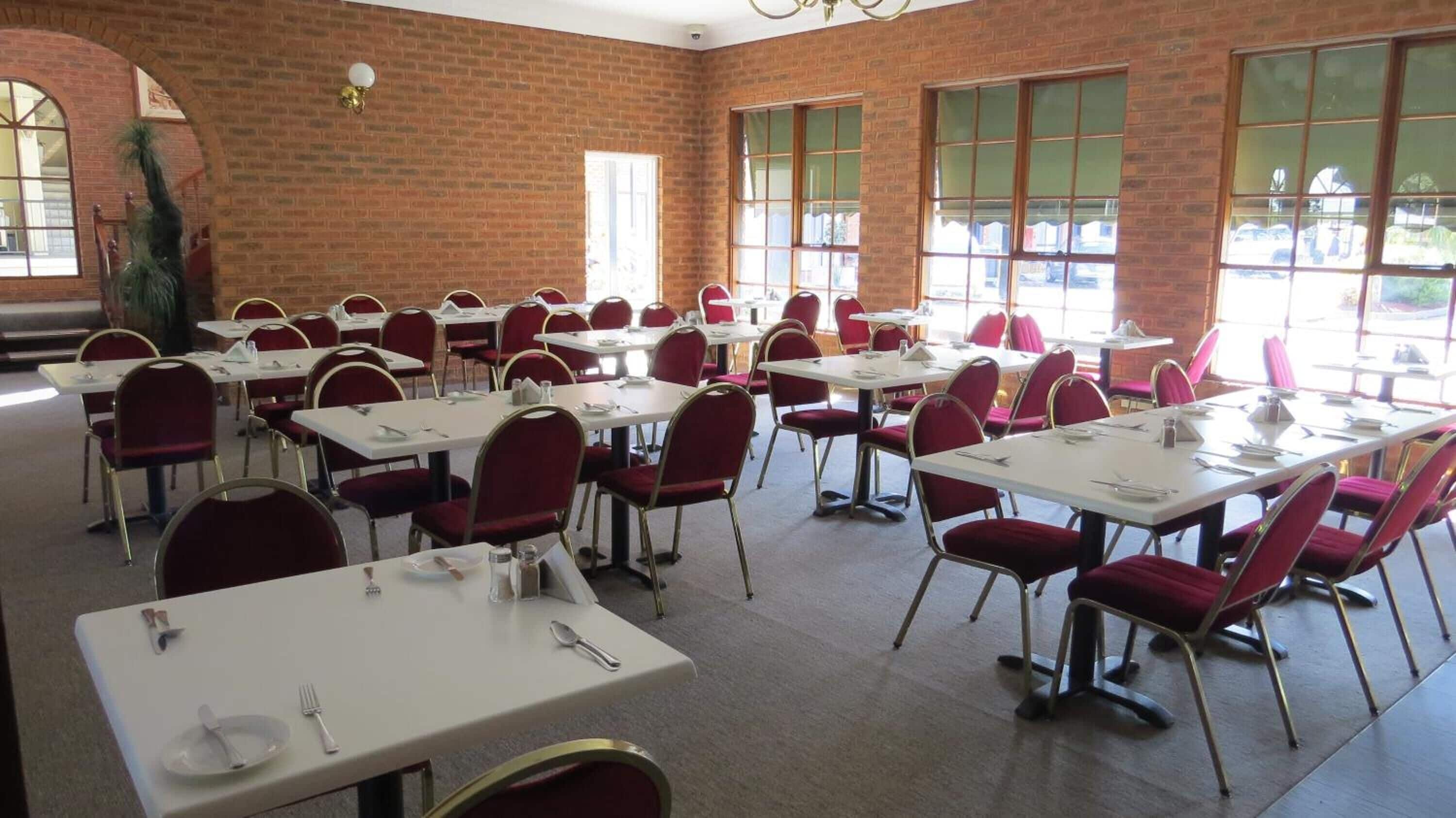 Uma sala de conferências com mesas e cadeiras, paredes de tijolo e janelas amplas.