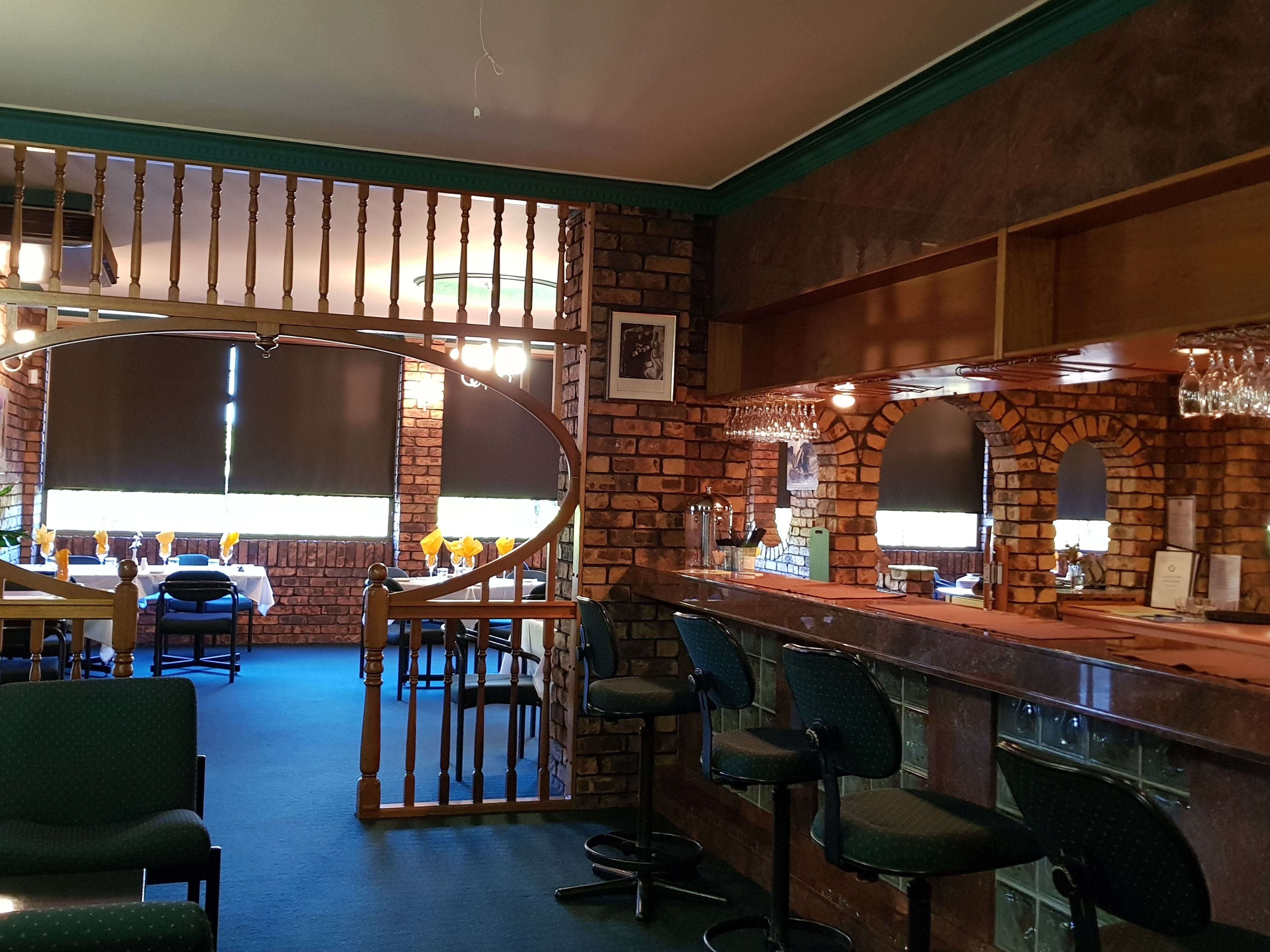 Um restaurante com paredes de tijolo, área de bar com banquetas e sala de jantar com mesas e cadeiras.