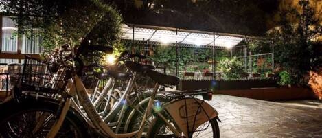 Bicicleta estacionada em área externa com área de estar coberta e plantas ao fundo.