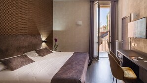 Quarto de hotel com uma cama grande, escrivaninha, cadeira, televisão e vista para o exterior.