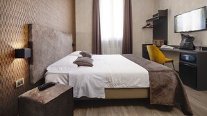 Quarto de hotel com cama, escrivaninha, cadeira, televisão e minibar.