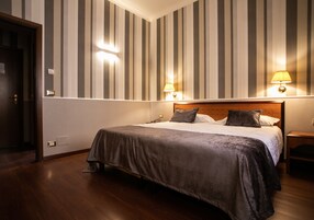 Quarto de hotel com uma cama grande, papel de parede listrado e duas luminárias de cabeceira.
