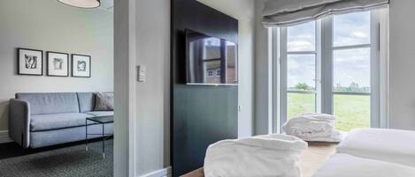 Quarto de hotel com sofá, televisão de tela plana, janela ampla com vista e mesa de massagem com toalhas.