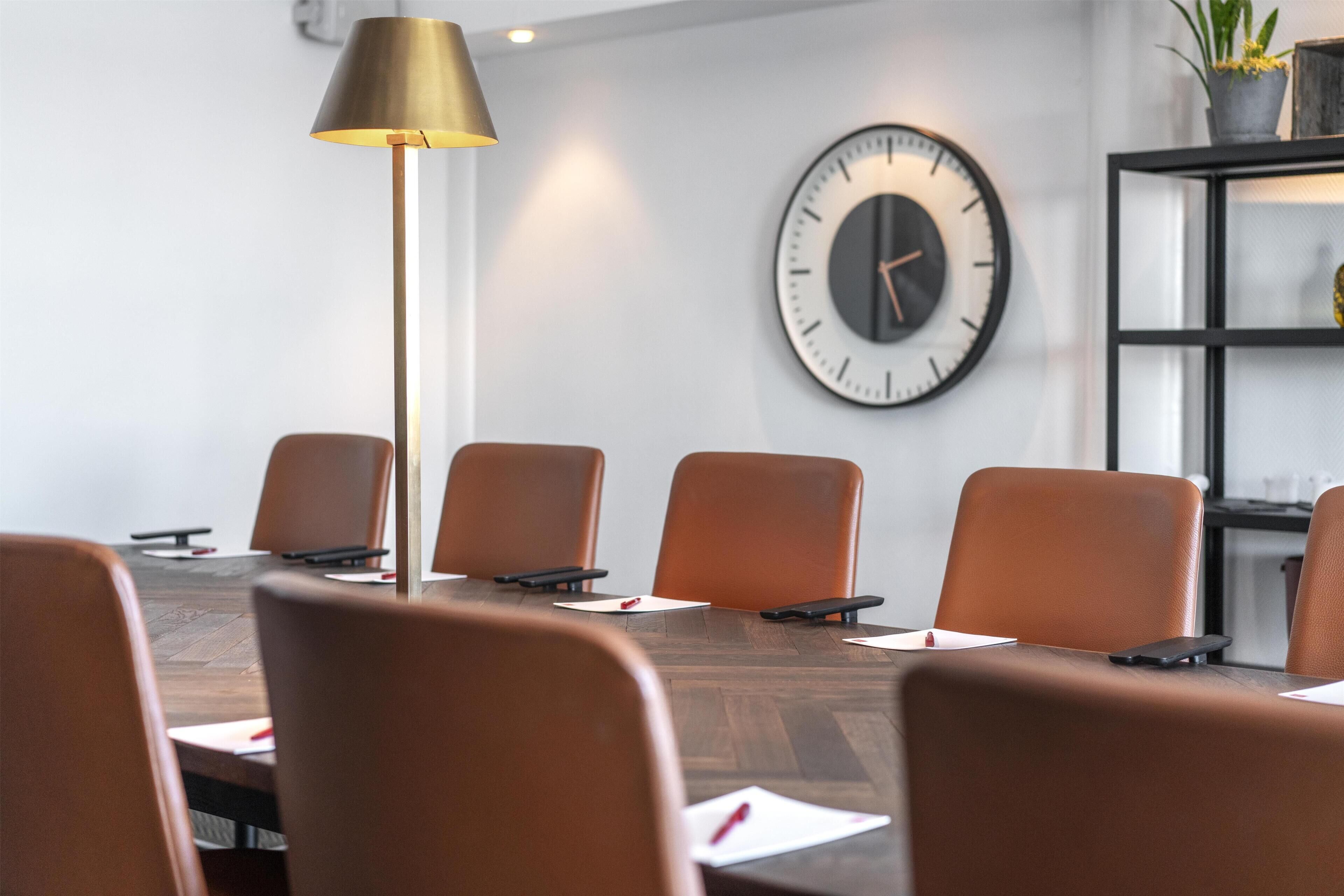 Uma sala de conferências com uma mesa comprida, seis cadeiras, um relógio na parede e um abajur.