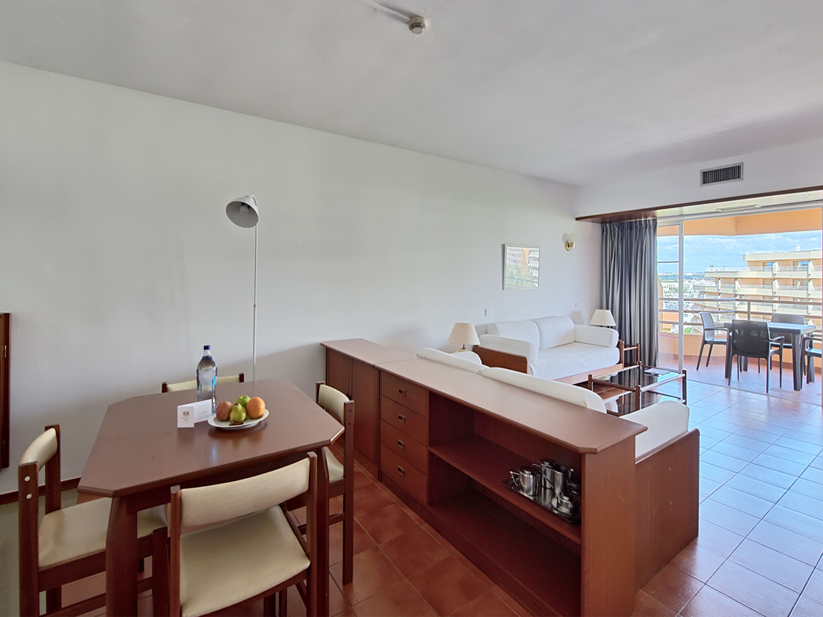 Quarto de hotel moderno com área de refeições, sofá e varanda com vista.