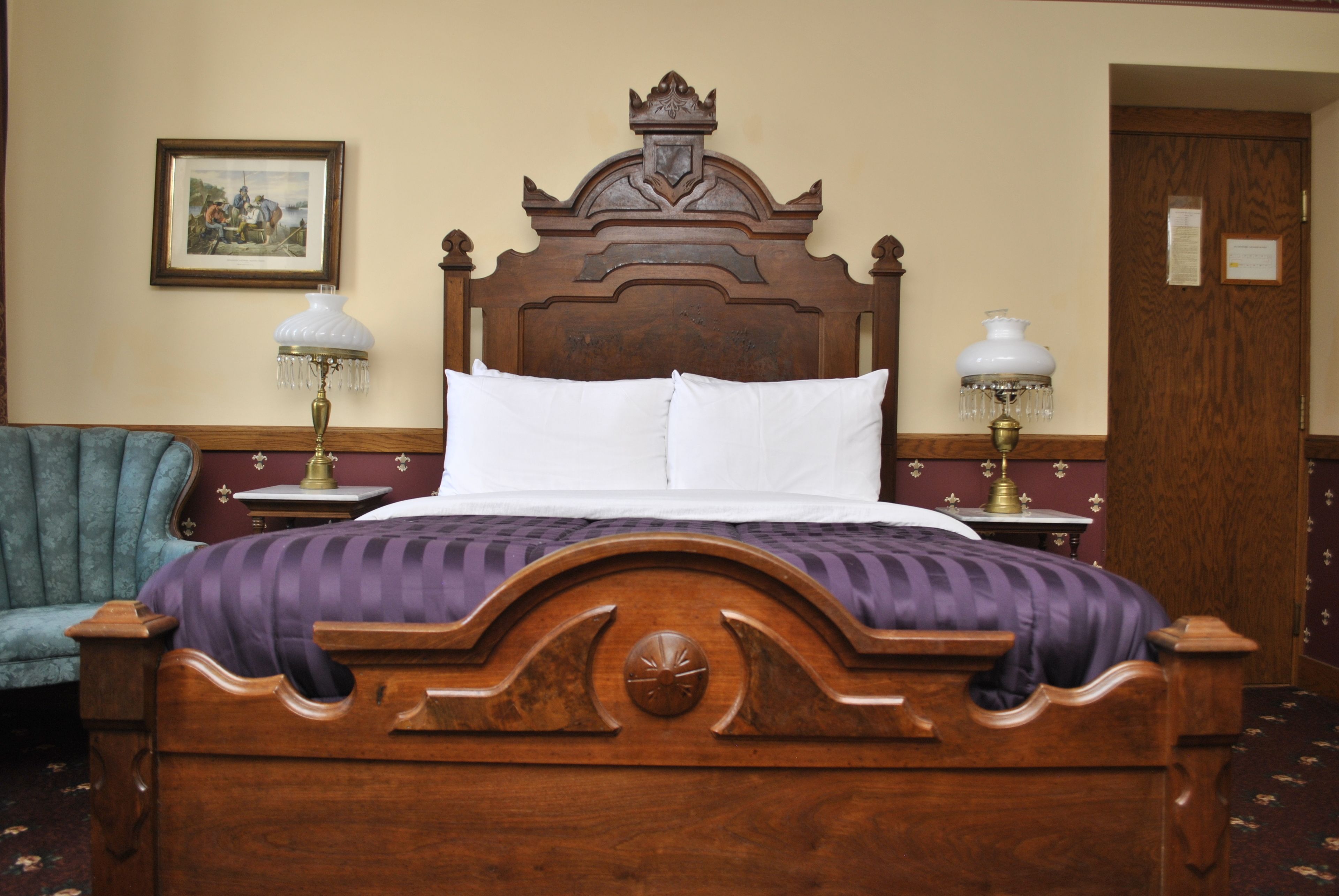 Uma cama de madeira com cabeceira decorativa, duas mesas de cabeceira com luminárias e um quadro na parede.
