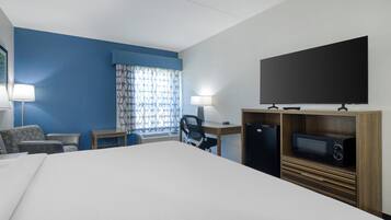 Quarto de hotel com uma cama grande, uma escrivaninha com computador, televisão, micro-ondas e uma cadeira.