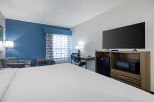 Quarto de hotel com uma cama grande, uma escrivaninha com computador, televisão, micro-ondas e uma cadeira.