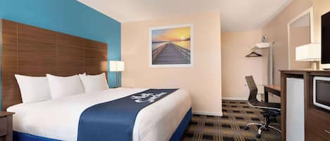 Quarto de hotel com uma cama grande, uma escrivaninha, uma cadeira e uma televisão.