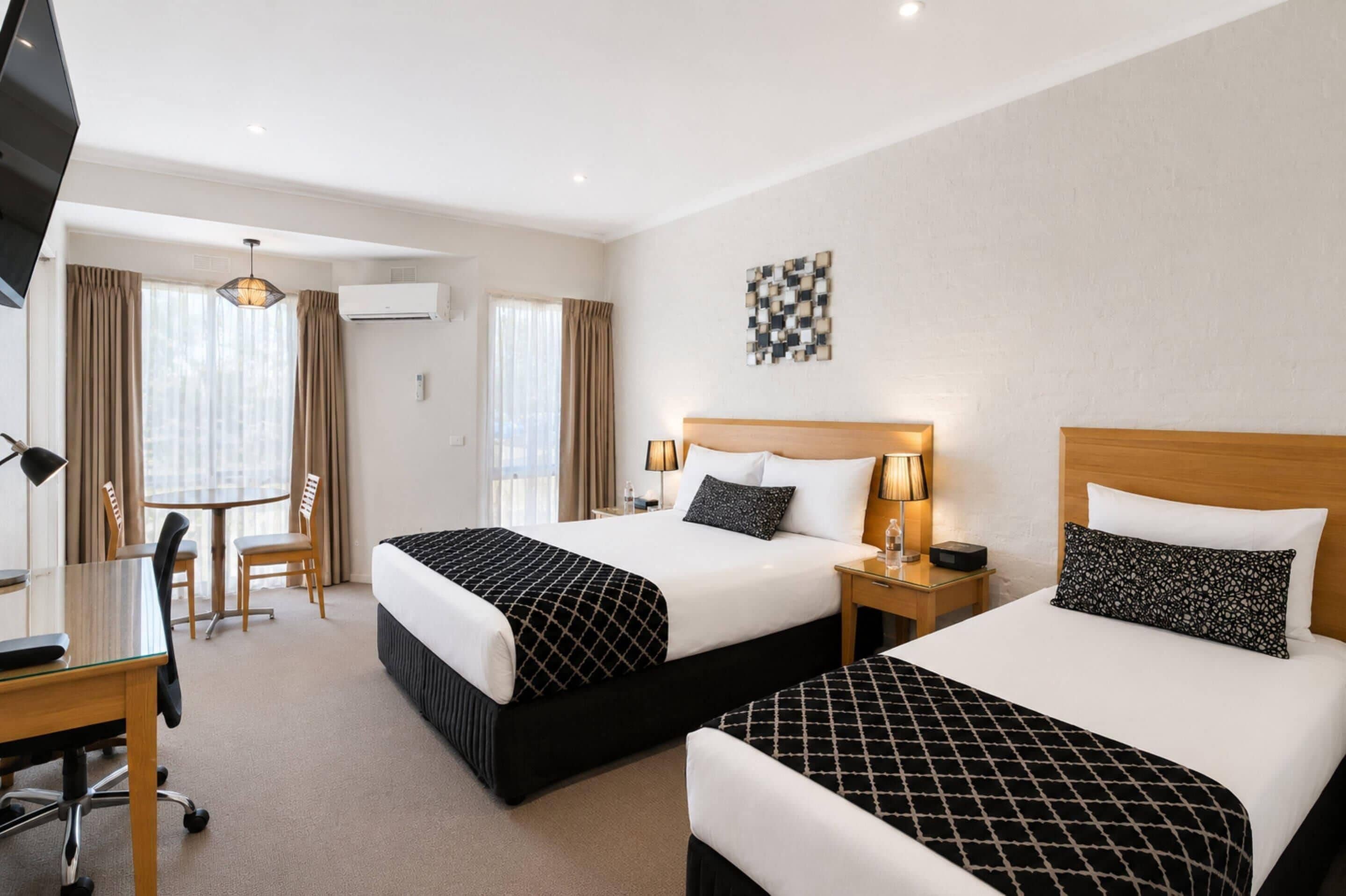 Quarto de hotel com duas camas, uma escrivaninha e uma cadeira.