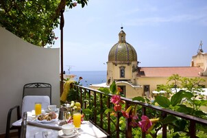 Varanda com mesa posta para café da manhã, com vista para a costa e uma igreja com cúpula.