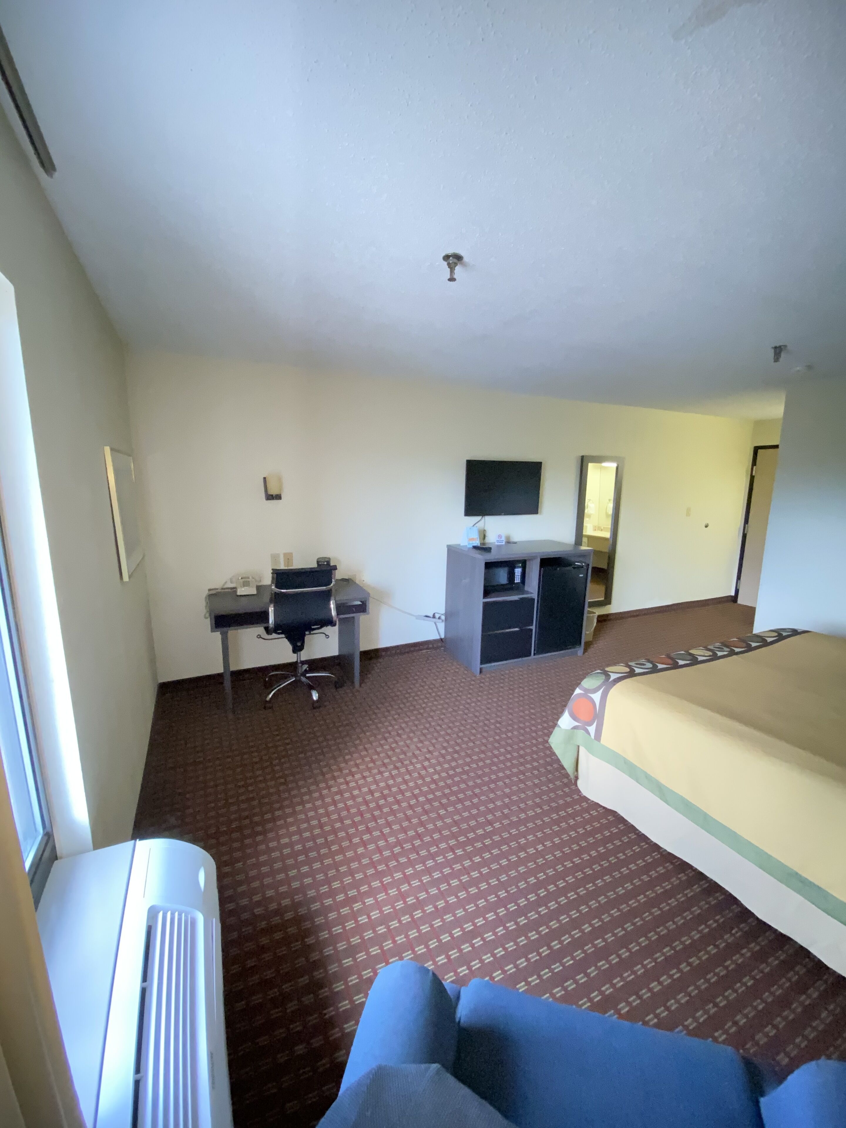 Quarto de hotel com cama, escrivaninha, cadeira, televisão e janela.