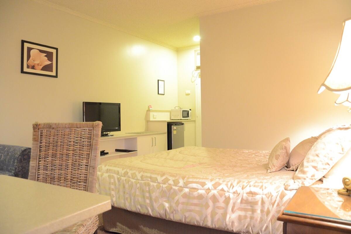 Um quarto com uma cama, televisão, escrivaninha e uma cadeira.
