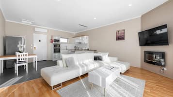 Uma sala de estar moderna com um sofá branco, uma mesa de jantar e uma cozinha ao fundo.