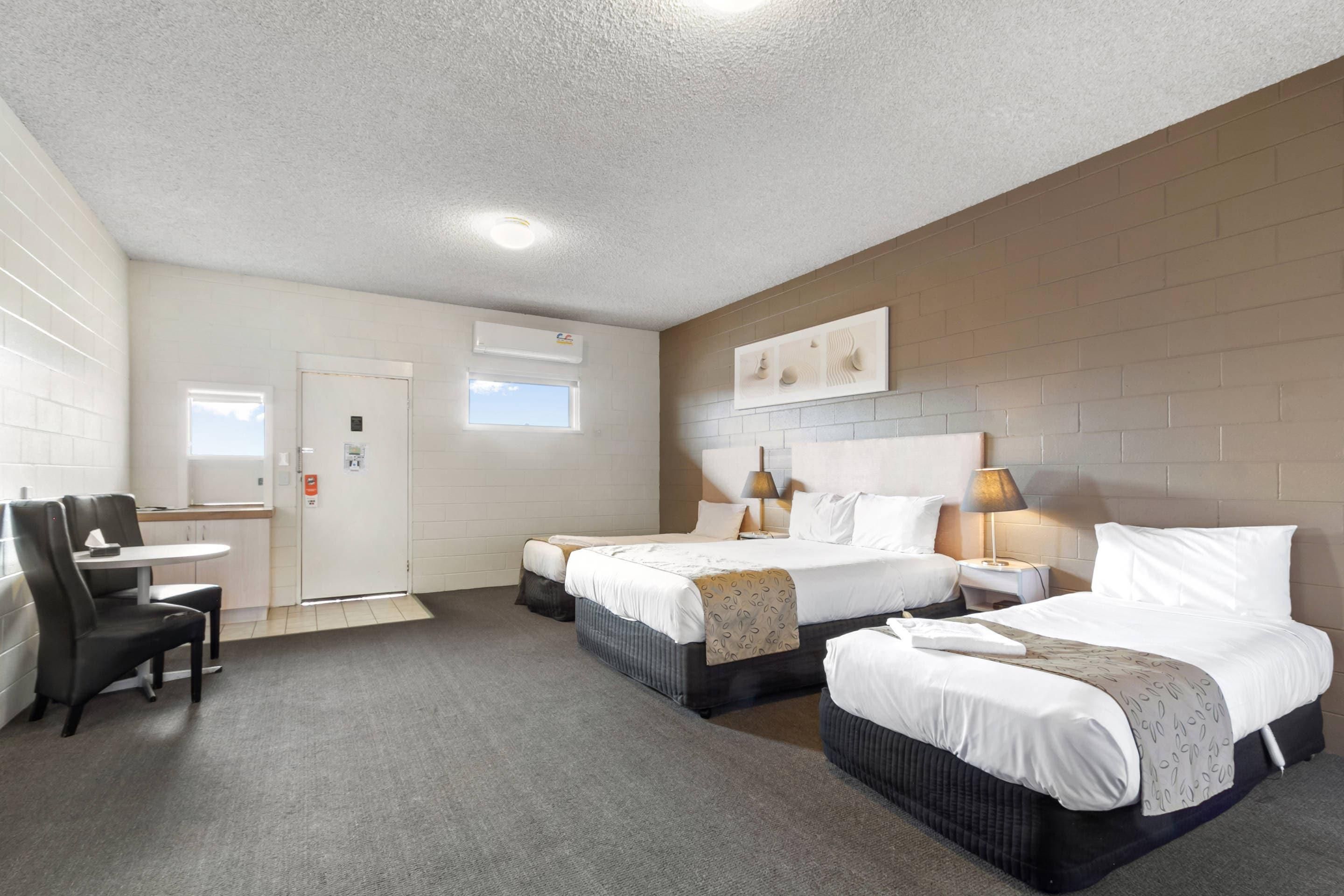 Quarto de hotel com duas camas, uma escrivaninha e uma cadeira. Possui duas janelas e um aparelho de ar condicionado na parede.