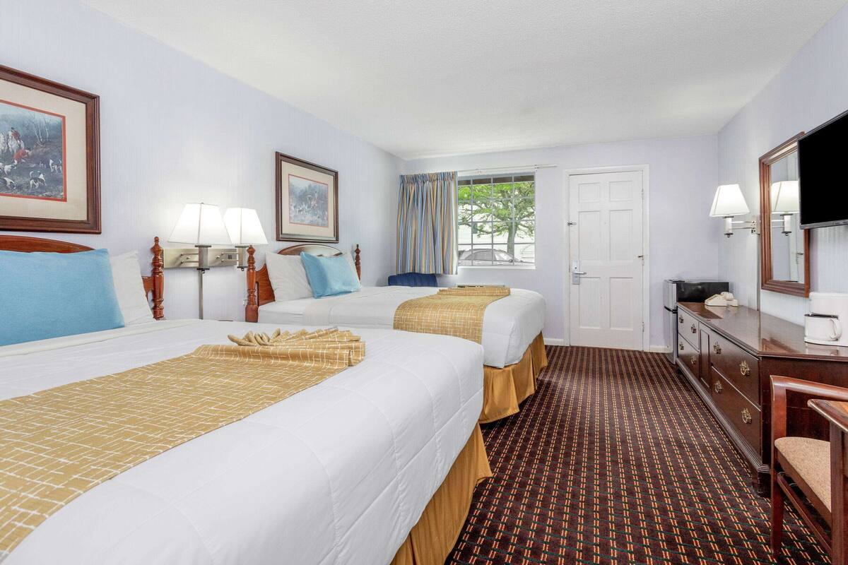 Quarto de hotel com duas camas, uma escrivaninha, uma cadeira, uma televisão e uma janela com cortinas.