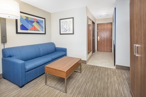Um quarto com um sofá azul, uma mesa de centro de madeira e duas obras de arte abstrata emolduradas na parede.
